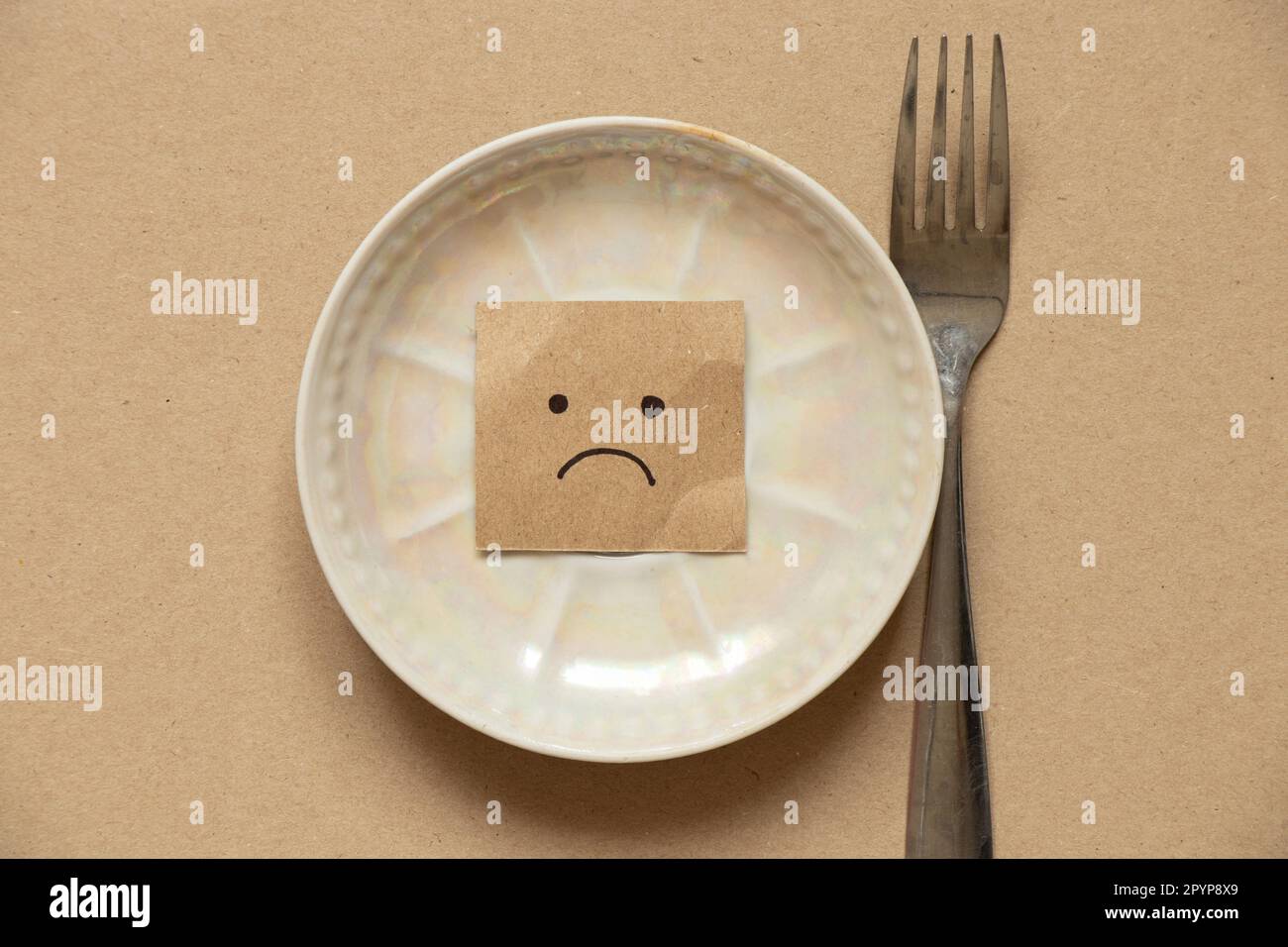 A sad emoticon drawn on a paper card lies on a plate, and next to it is ...