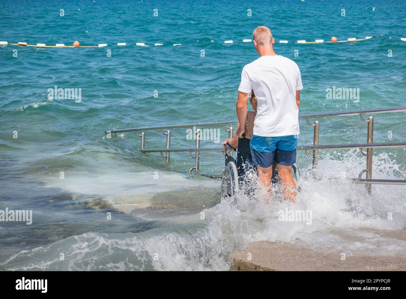 Woman with disability on wheelchair at accessible beach goes swimming ...