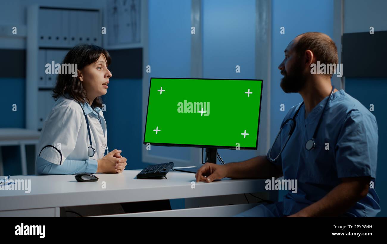 Medic and assistant looking at computer monitor with green screen ...