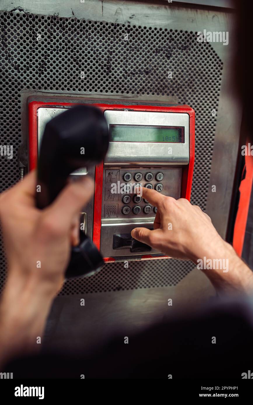 Person dialing a phone number on a public telephone at a payphone booth ...