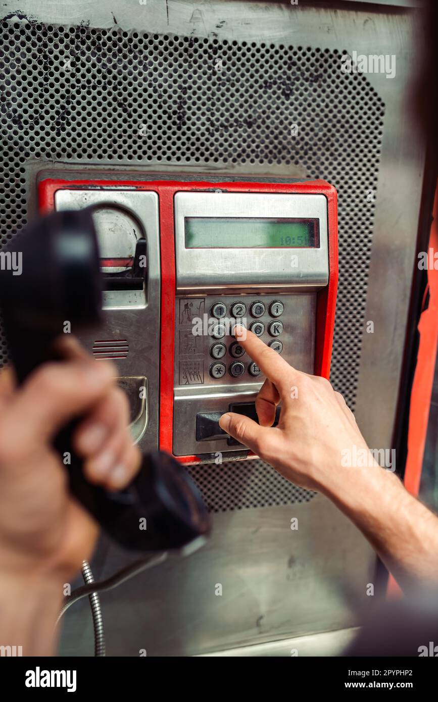 Person dialing a phone number on a public telephone at a payphone booth ...
