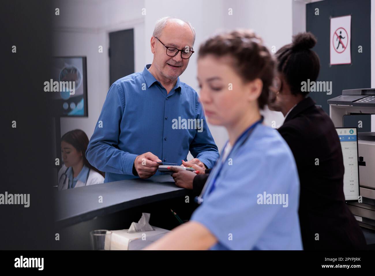 Senior patient standing at registration counter paying with credit card ...