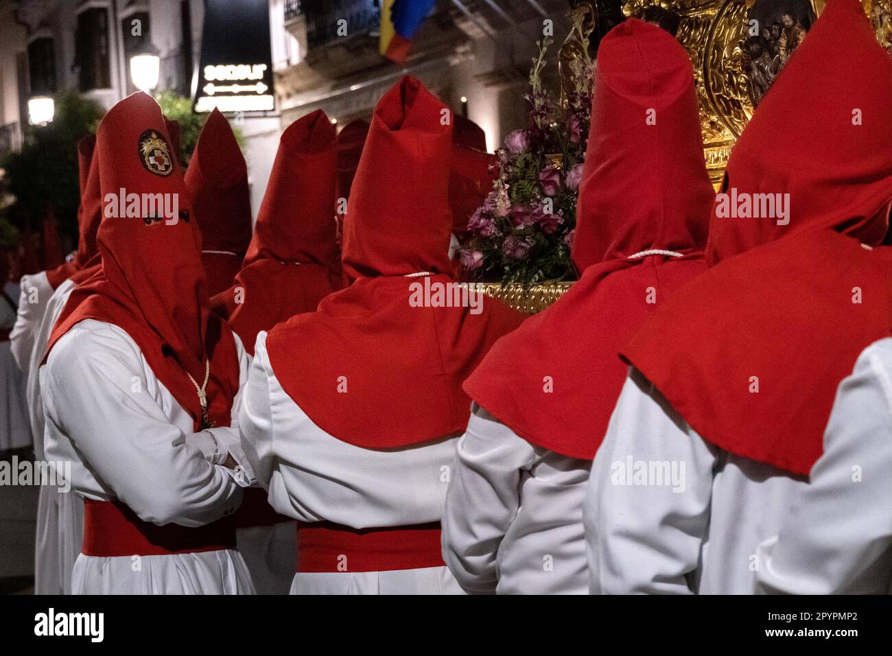 A Nazareno wearing a red hood looks back as he carries a massive ...