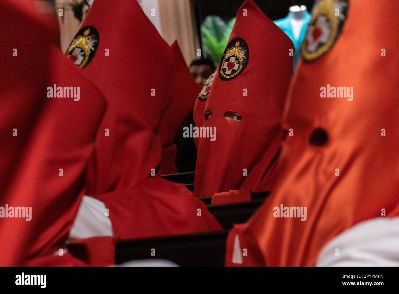 A Nazareno wearing a red hood looks back as he carries a massive ...
