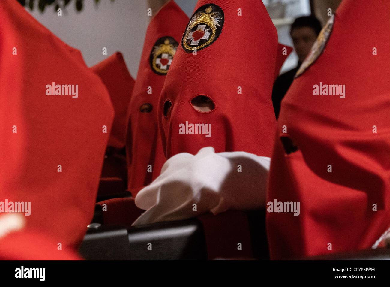 A Nazareno wearing a red hood looks back as he carries a massive ...