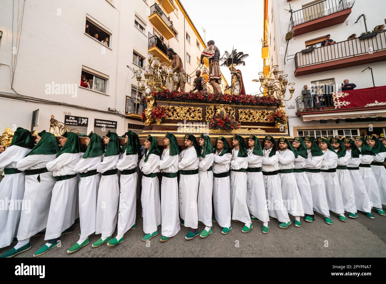 Nazarenos wearing green hats carry a massive platform with a statue of ...