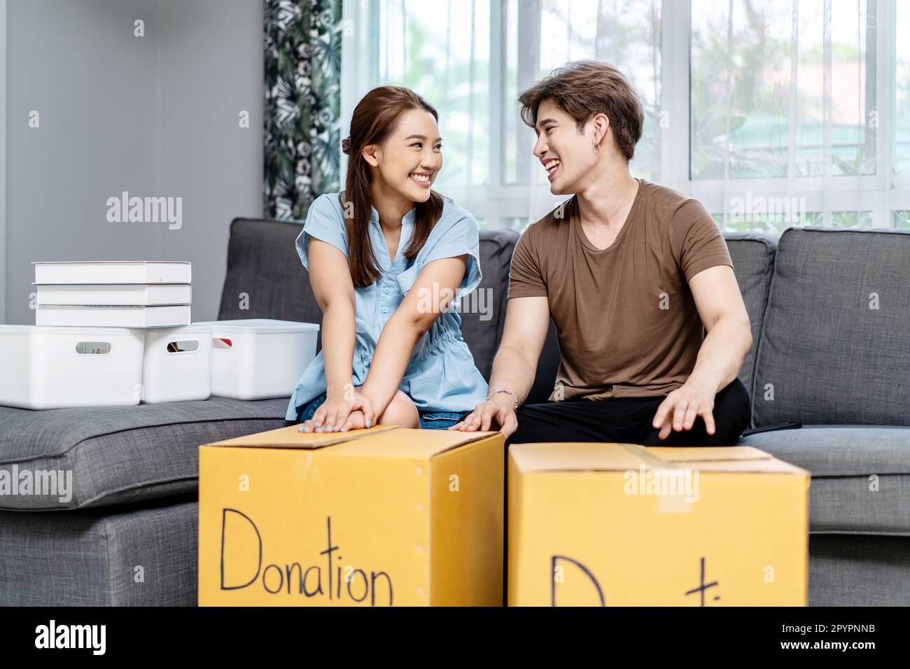 Portrait happy young couple packing stuff clothes, object charity in cardboard box, reused for ...