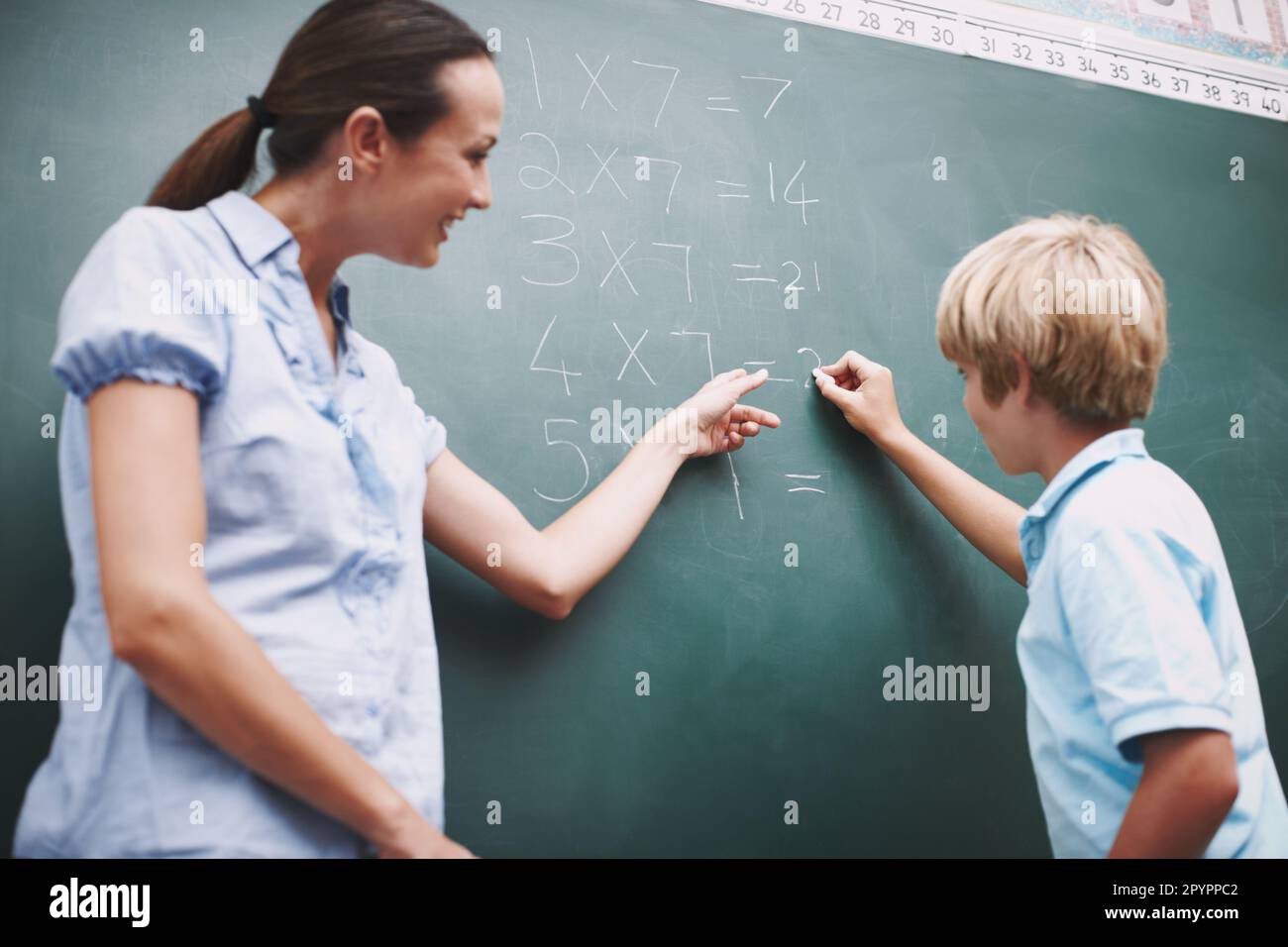 Helping him with his sums. A pretty teacher standing at the blackboard ...