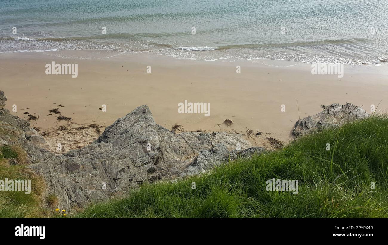 View of a beach with gentle waves looking from a grassy cliff edge ...