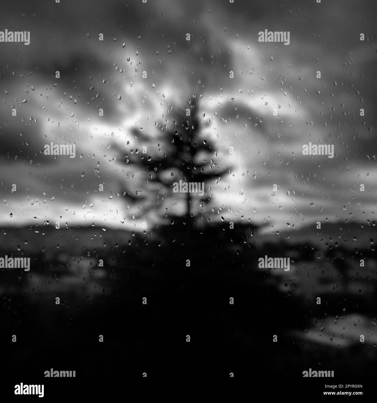 Raindrops in focus on window pane looking out towards horizon with dark ...