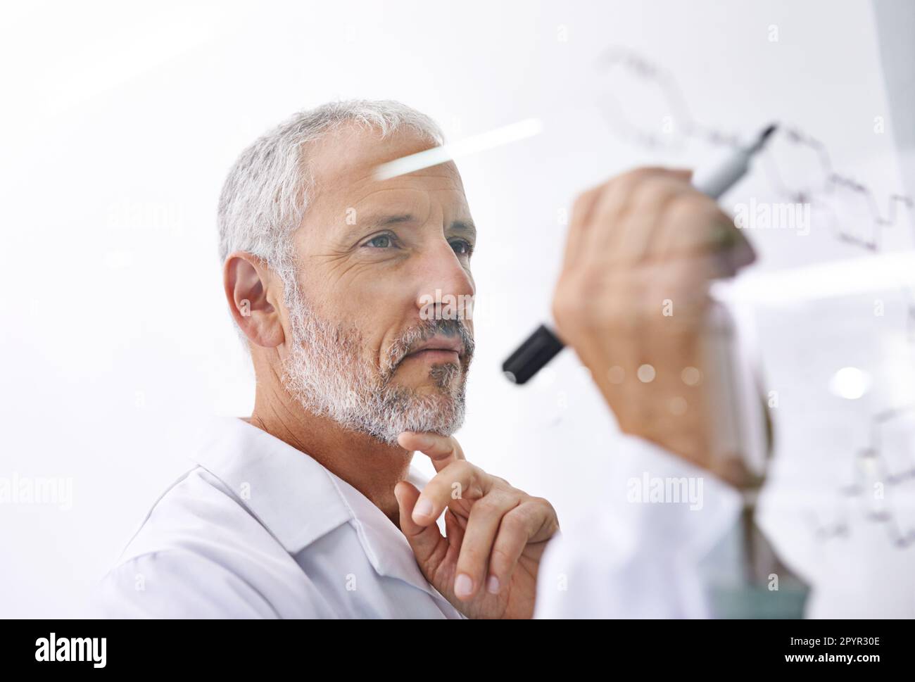 Analyzing the chemical bonds. a mature male scientist drawing a molecular structure on a glass ...