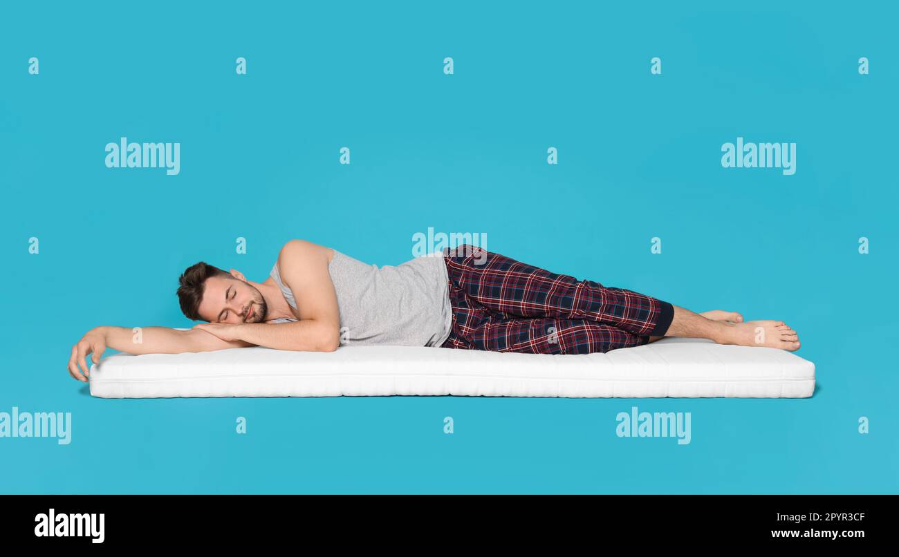 Man sleeping on soft mattress against light blue background Stock Photo ...