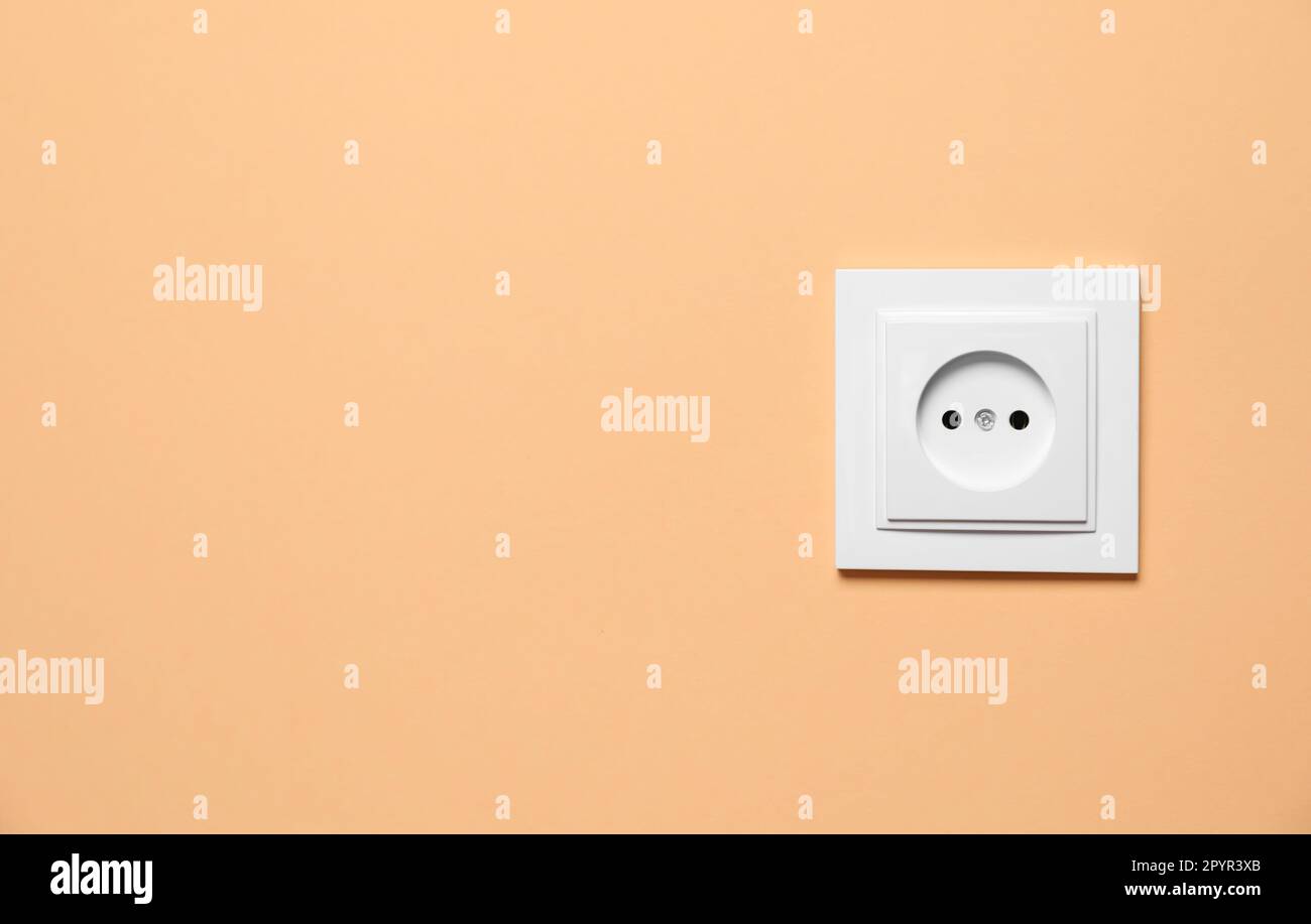Power socket on pale orange wall, space for text. Electrical supply ...