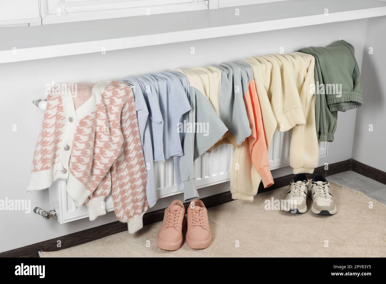 Heating radiator with clothes and shoes in room Stock Photo - Alamy