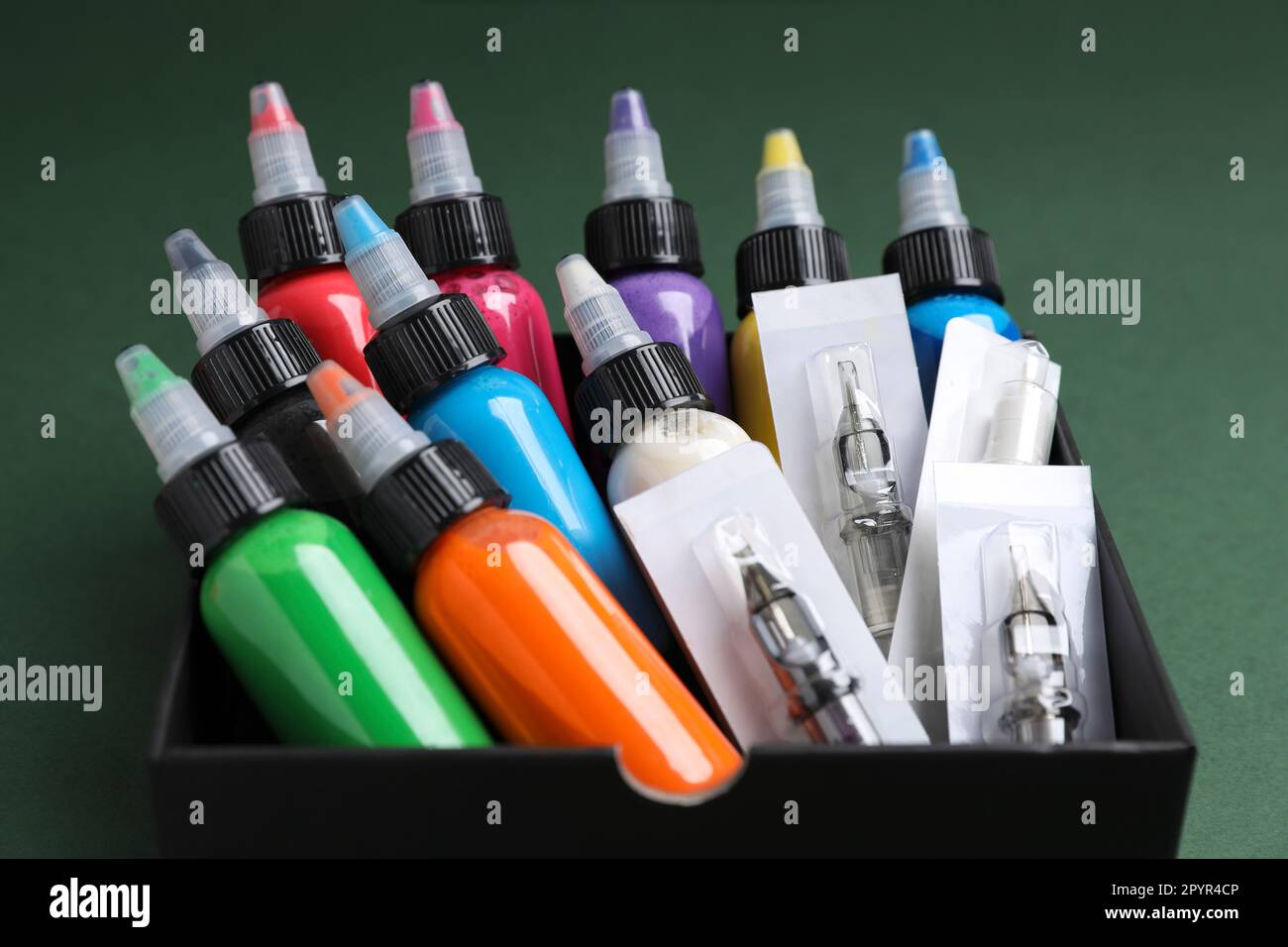 Box with colorful tattoo inks and needle cartridges on dark green ...