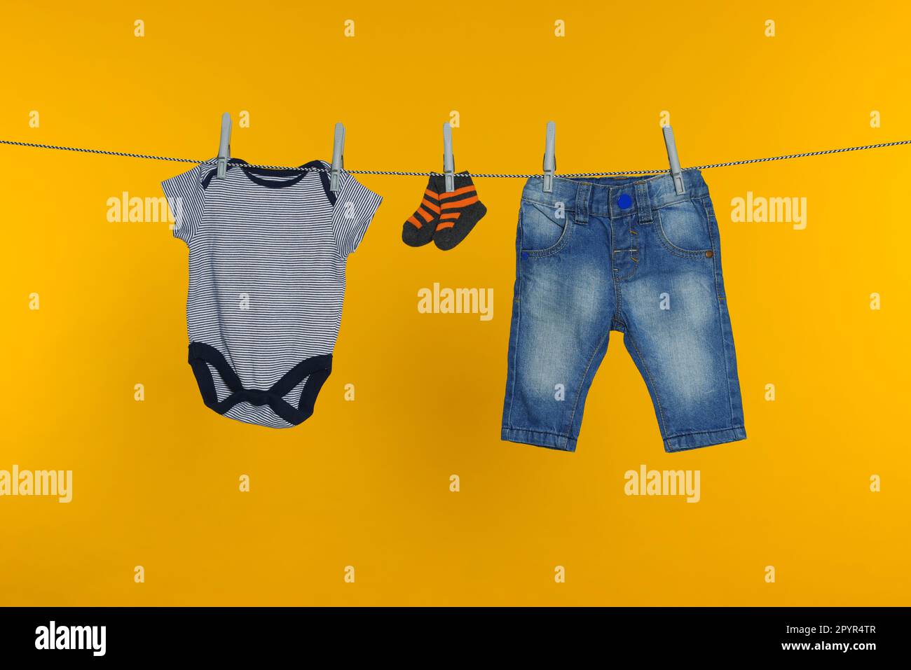Different baby clothes drying on laundry line against orange background ...