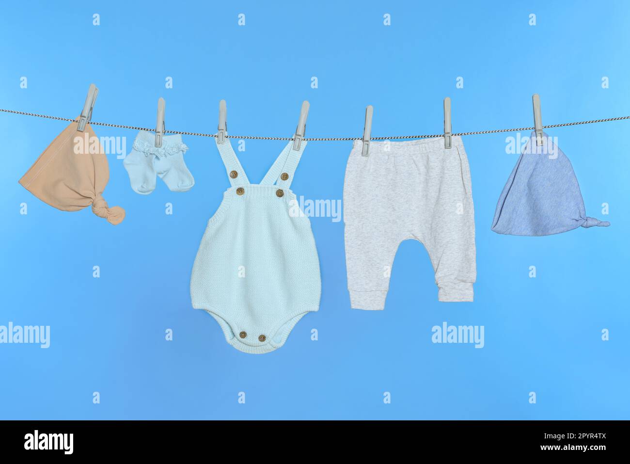 Different baby clothes drying on laundry line against light blue ...