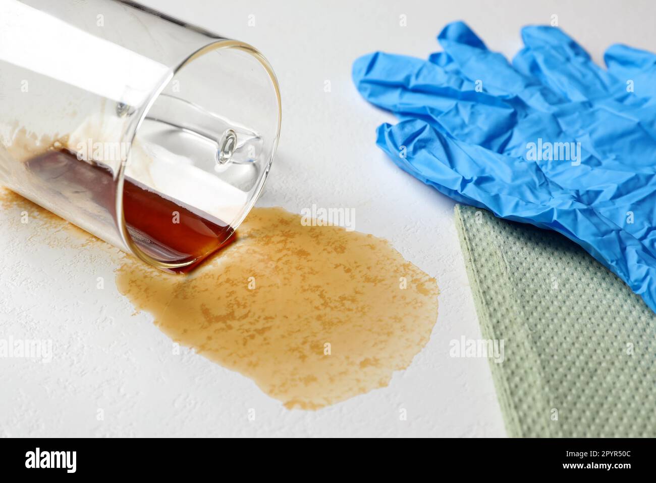 Glove, paper towel, overturned cup and spilled coffee on light table ...