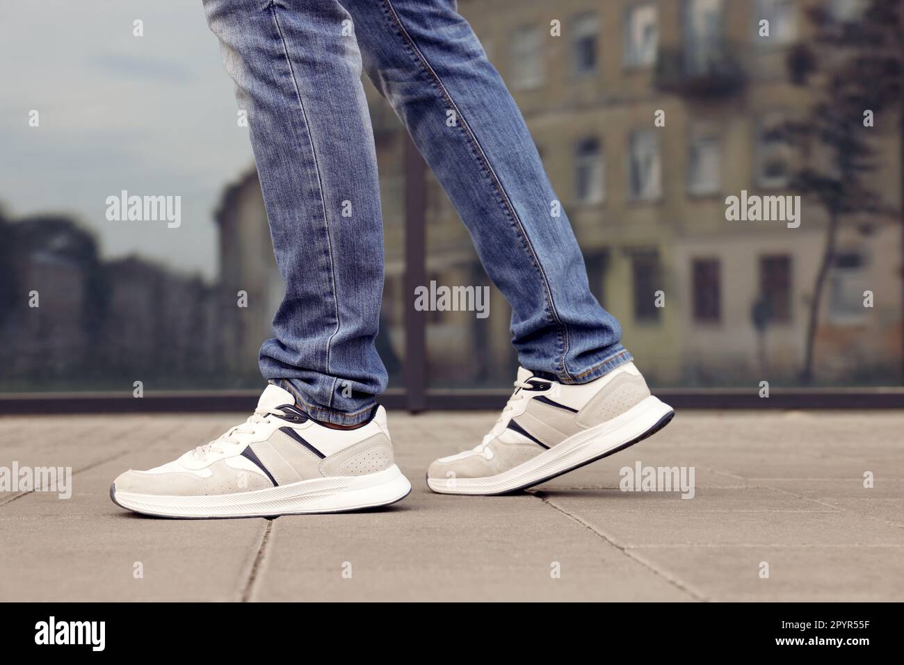 Man in jeans and sneakers walking on city street, closeup. Space for ...