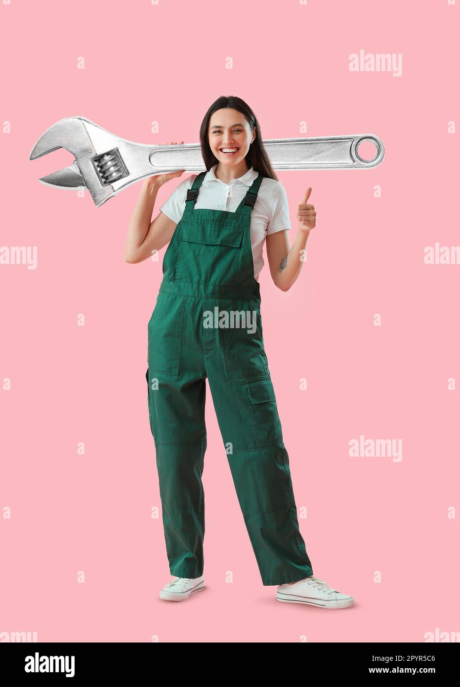 Female worker with big adjustable wrench showing thumb-up on pink ...