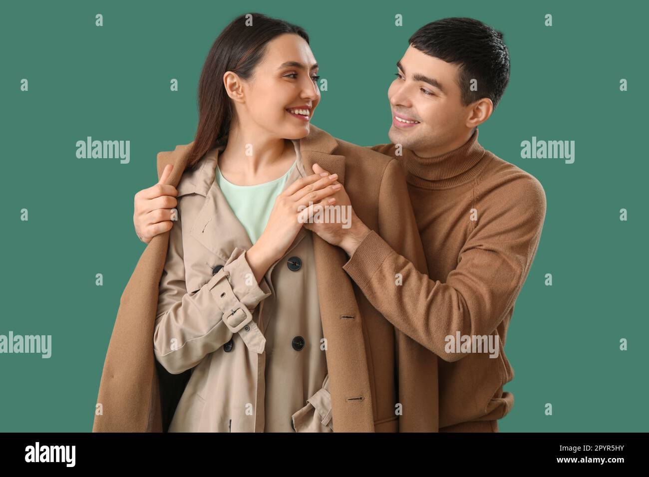Young man putting coat onto his girlfriend on green background Stock ...