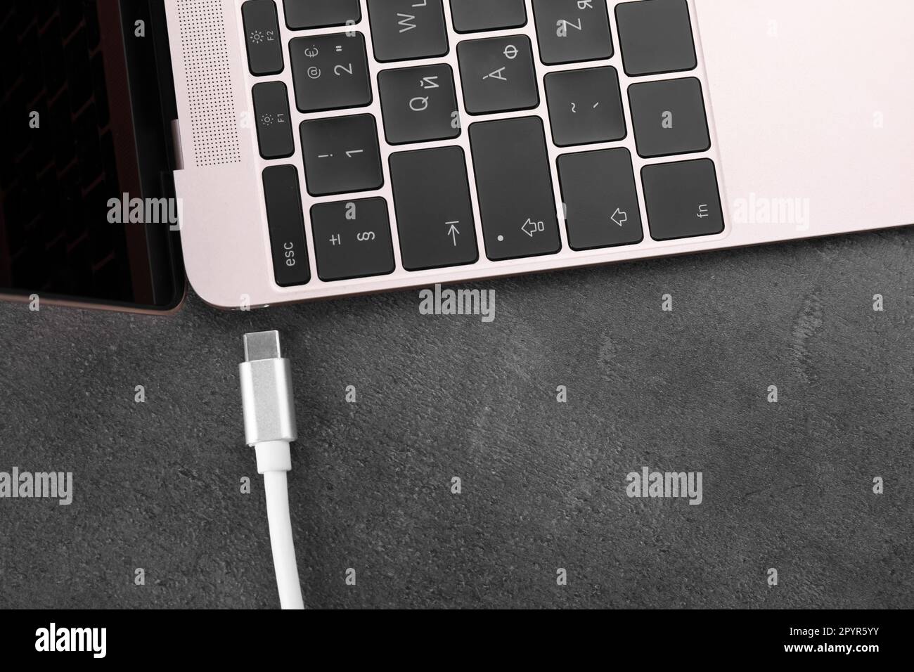 USB cable with type C connector and laptop on dark table, top view ...