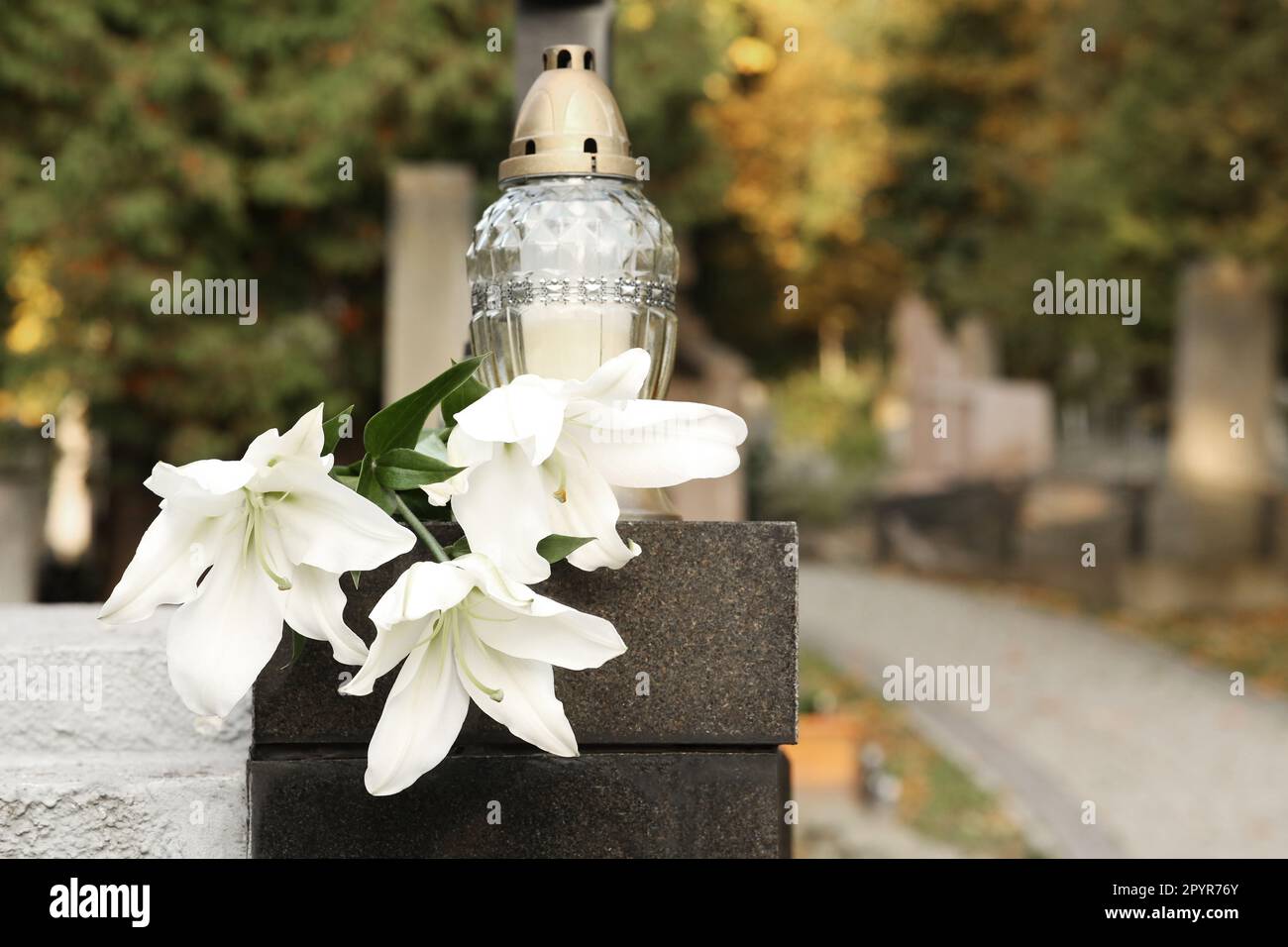 White lilies and grave light on grey granite tombstone outdoors, space for text. Funeral ...