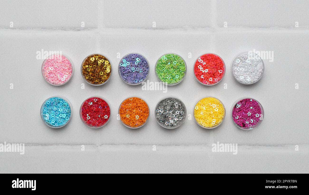 Many different colorful sequins in containers on white tiled background ...