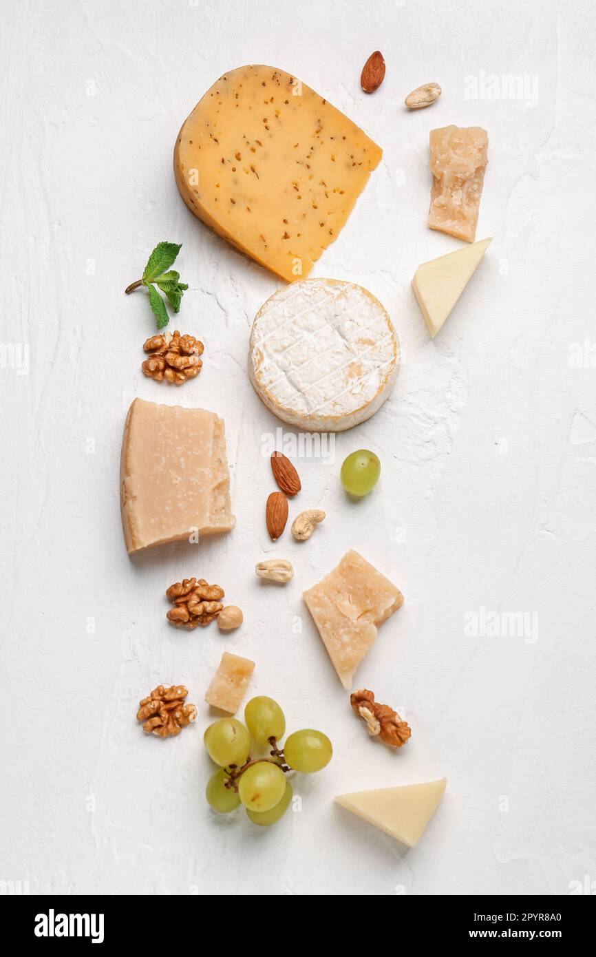 Different types of tasty cheese, nuts and grapes on light background ...