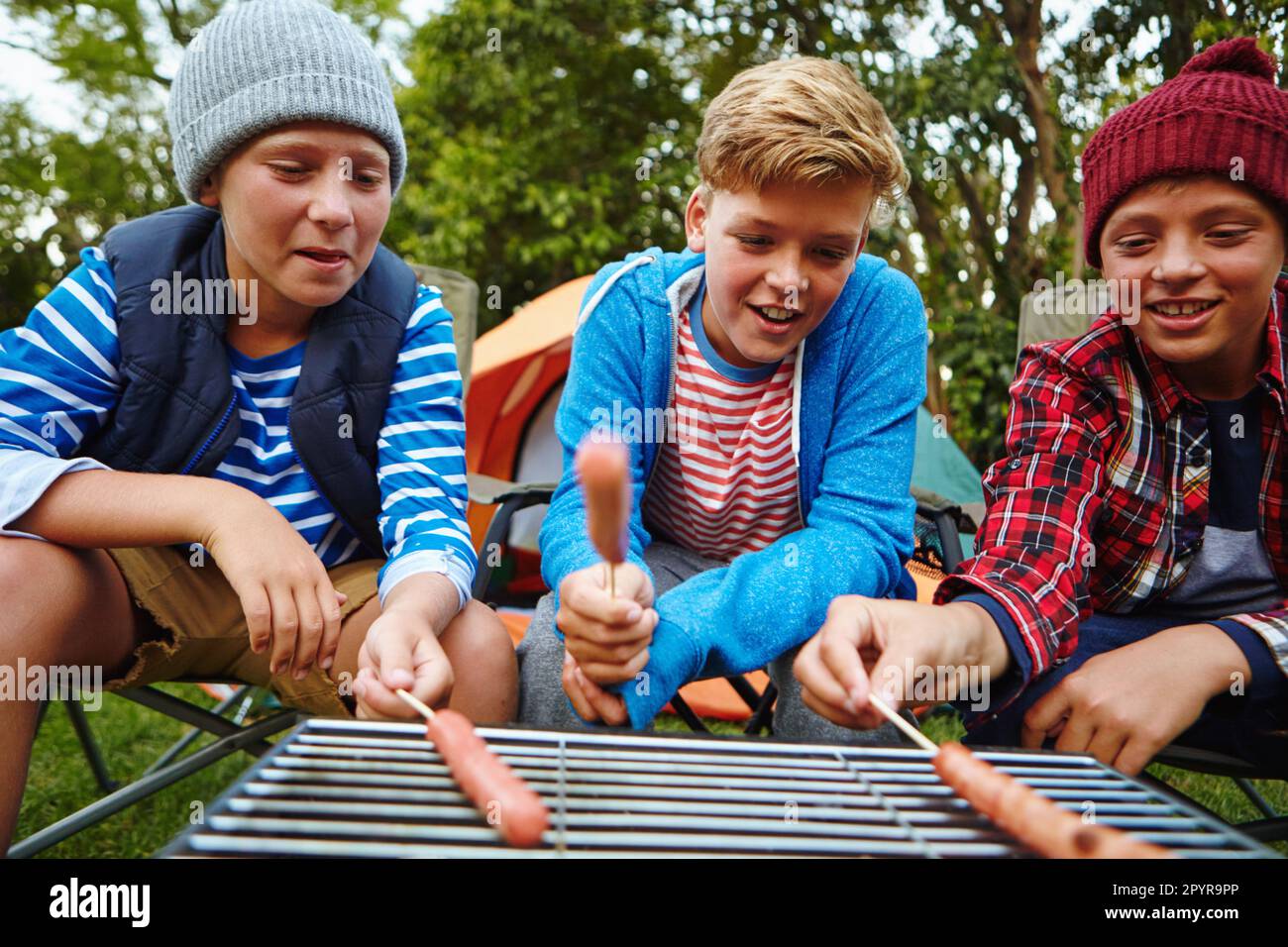 Grill em up boys. a three boys roasting hotdogs on a grill while ...