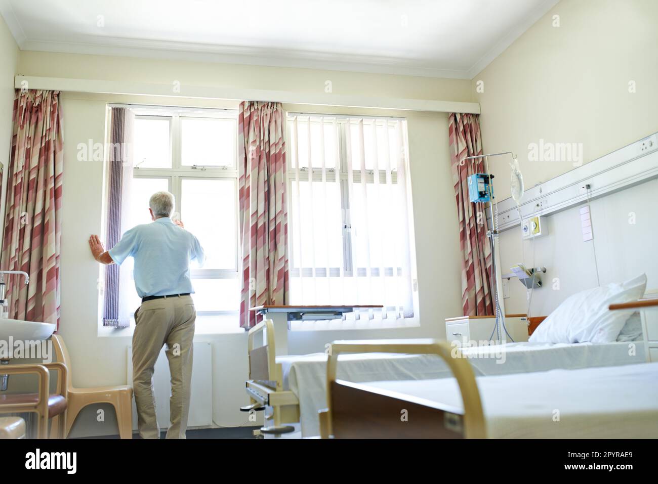 Taking his mind off the wait. a senior man looking out a window while ...