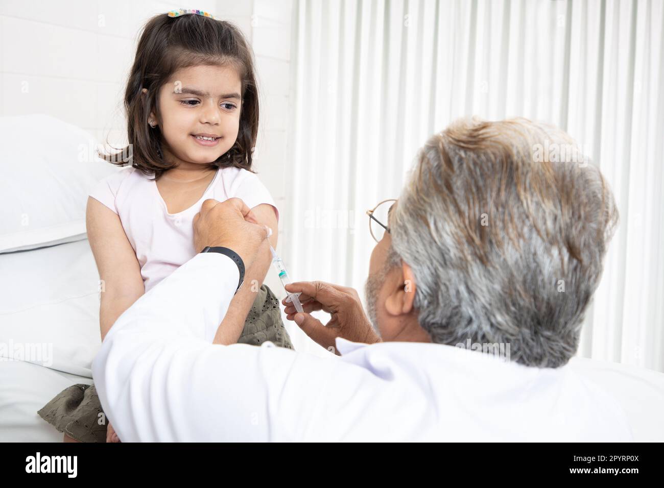 Senior Indian man pediatrician performs a vaccination of a little girl ...
