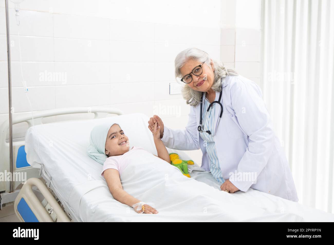 Smiling indian senior woman doctor holding hand of little girl cancer ...