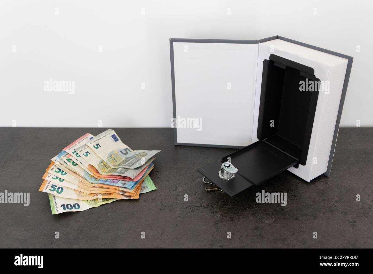 An opened fake book safe with a fan of cash, including 100 euro bills ...