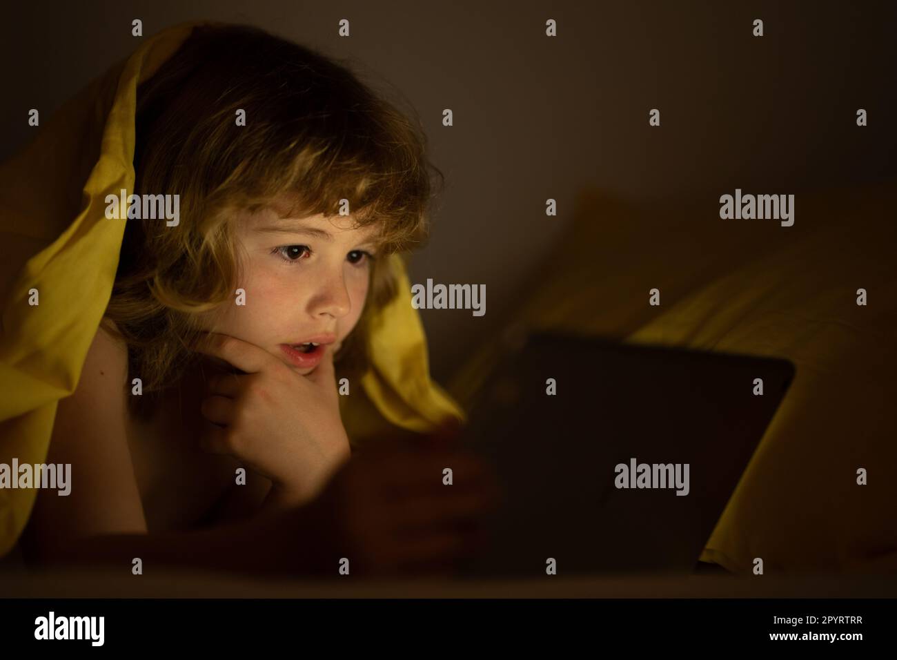Kid boy lying on bed and surfing Internet on tablet in dark room. Child ...