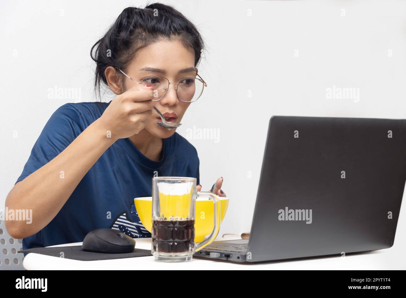 Young woman is eating at the computer Stock Photo - Alamy