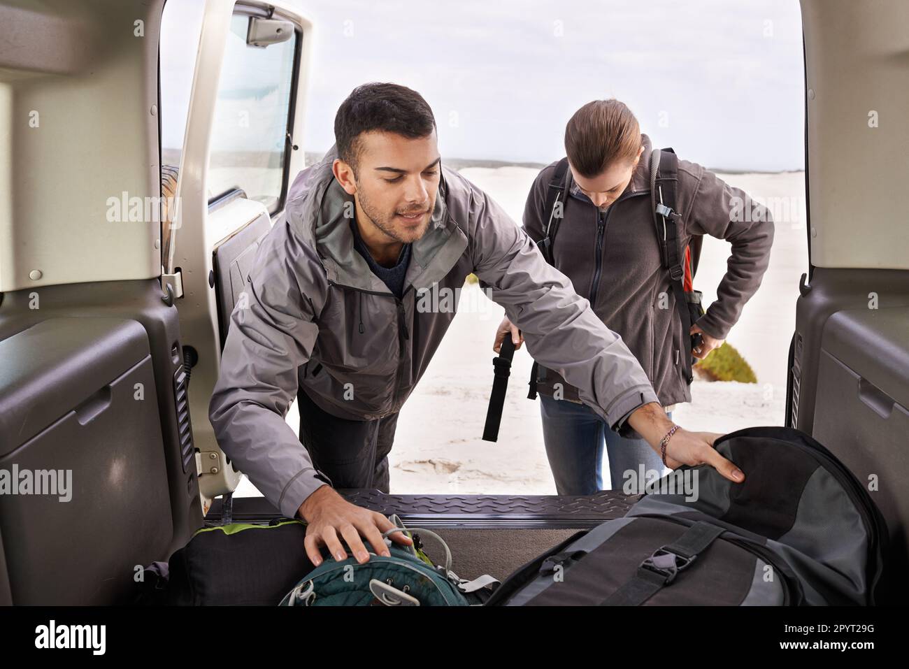 Lemme just grab the gear. a young couple at the back of their car while ...