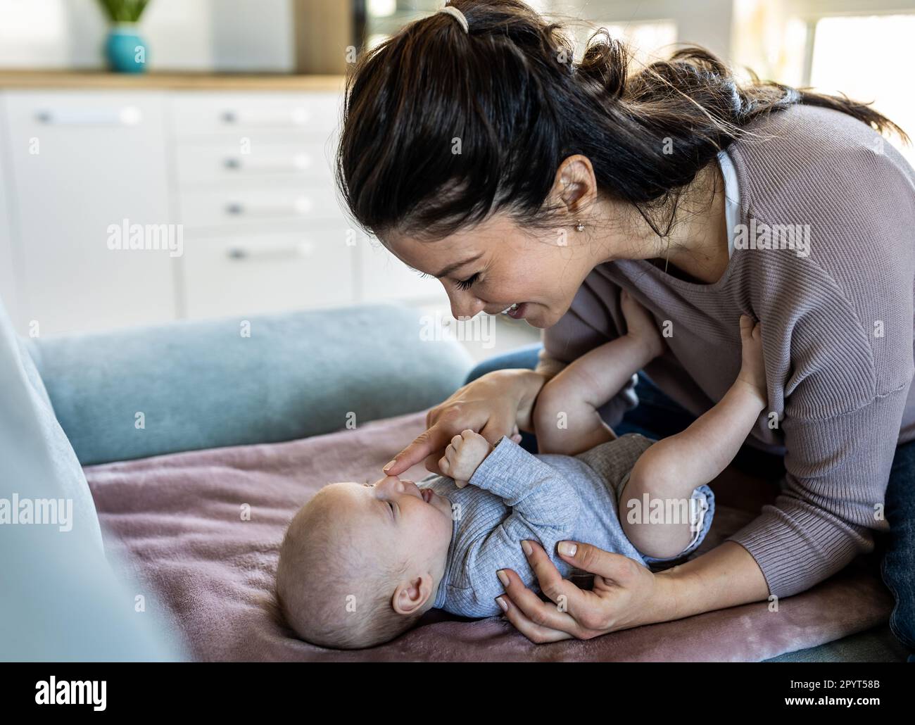 Cute newborn baby lying on back and smiling at mother on bed at home ...