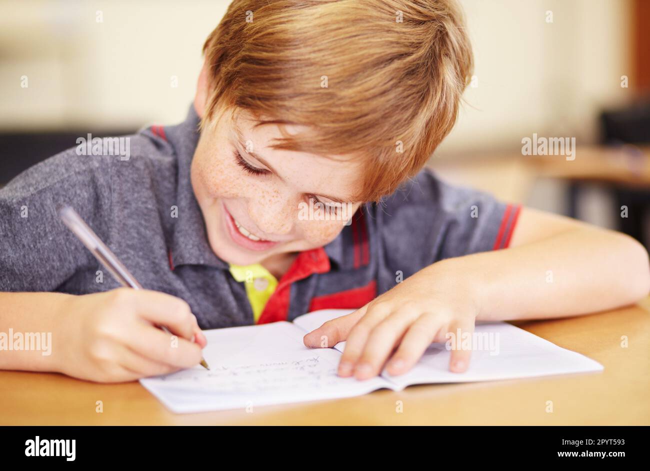 School, education and a student boy writing in a book while sitting at ...