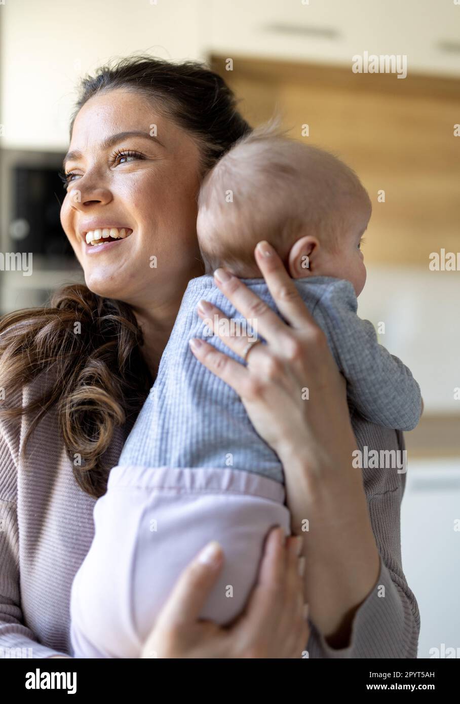 Smiling pretty mum holding infant on shoulder and enjoying tender ...