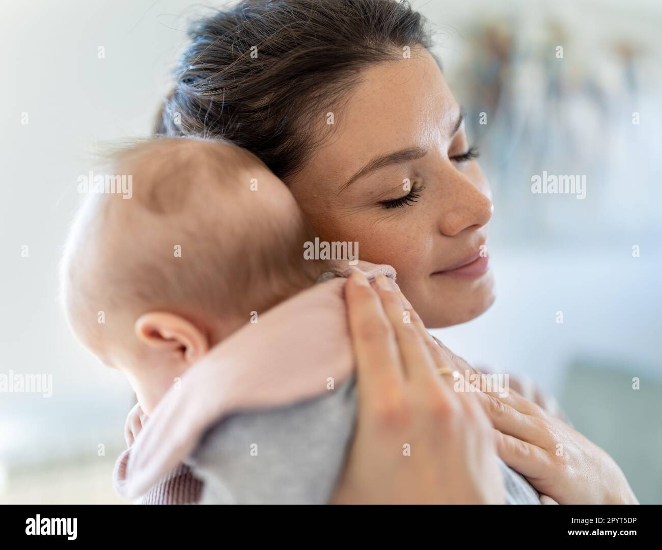 Smiling pretty mum holding infant on shoulder and enjoying tender quiet ...