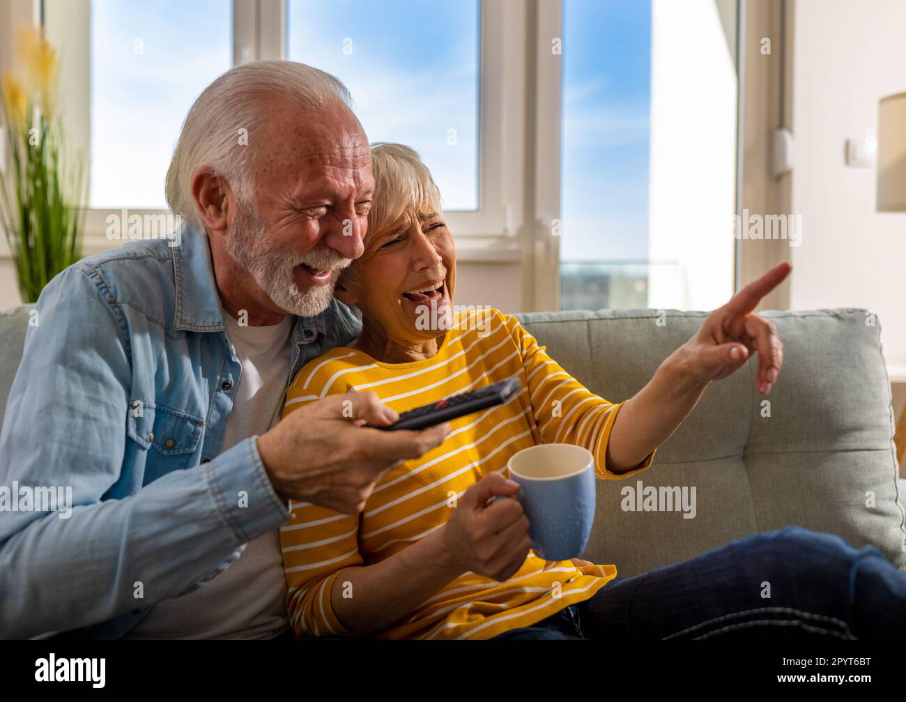 Senior couple watching funny scenes in movie and laughing on sofa at ...