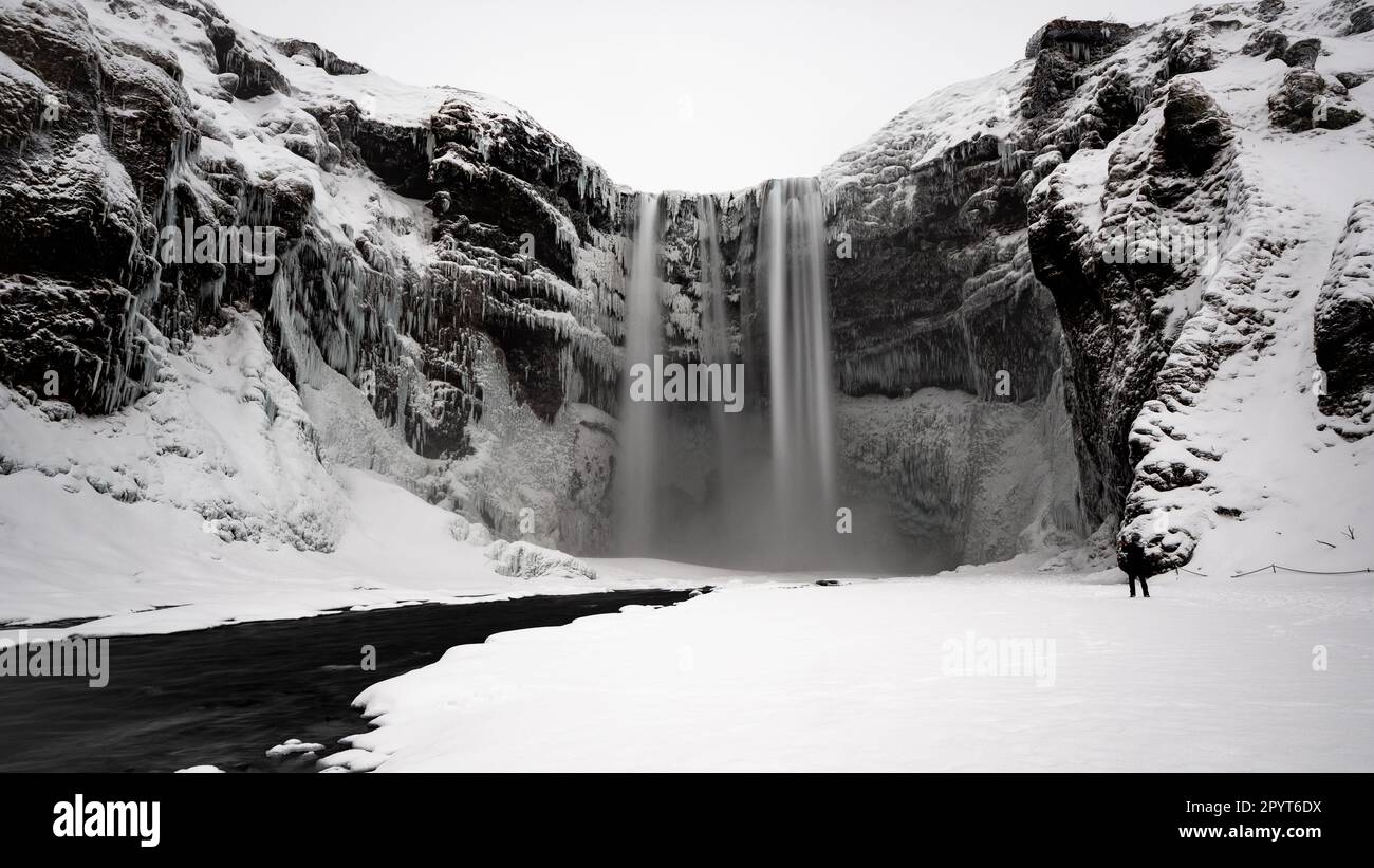 Man standing in front of famous frozen Iceland waterfall Stock Photo ...