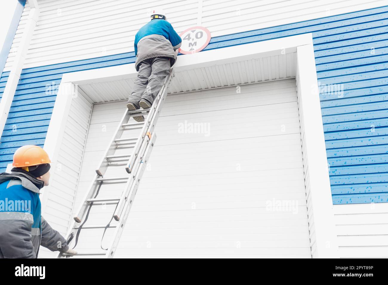 Two construction workers fix sign on automatic garage door for large ...