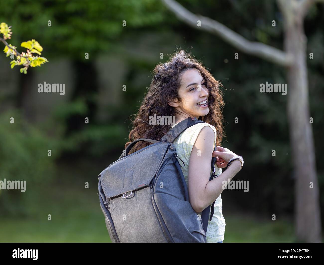 Pretty teenage girl with long curly hair holding backpack and looking ...