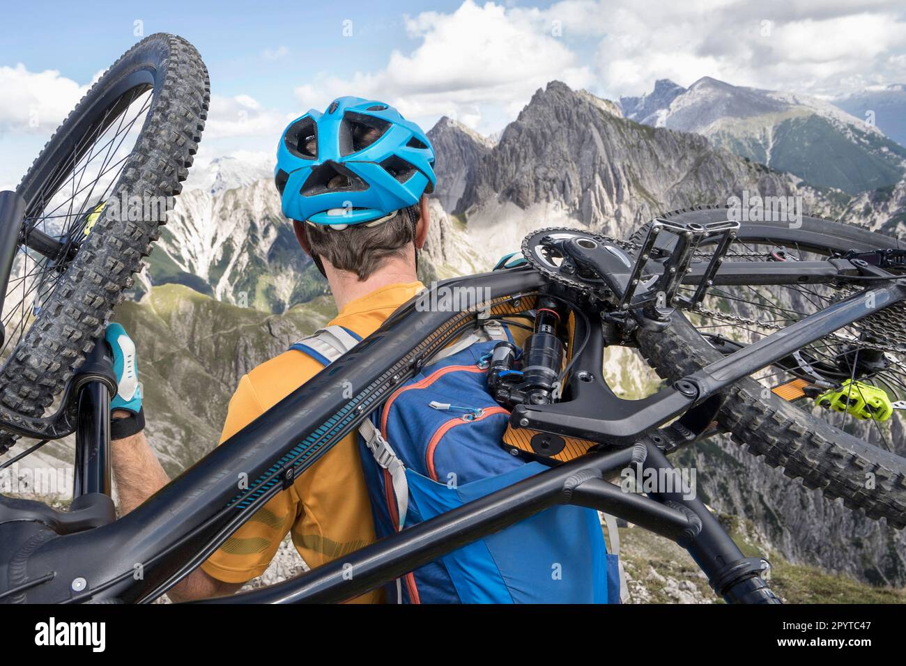 Rear view of a mountain biker carries his bike on shoulder and walking ...