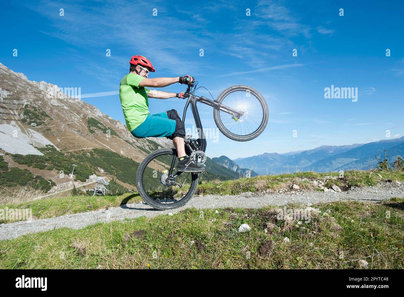 Mountain biker riding on back wheel through mountain, Tirol, Austria ...