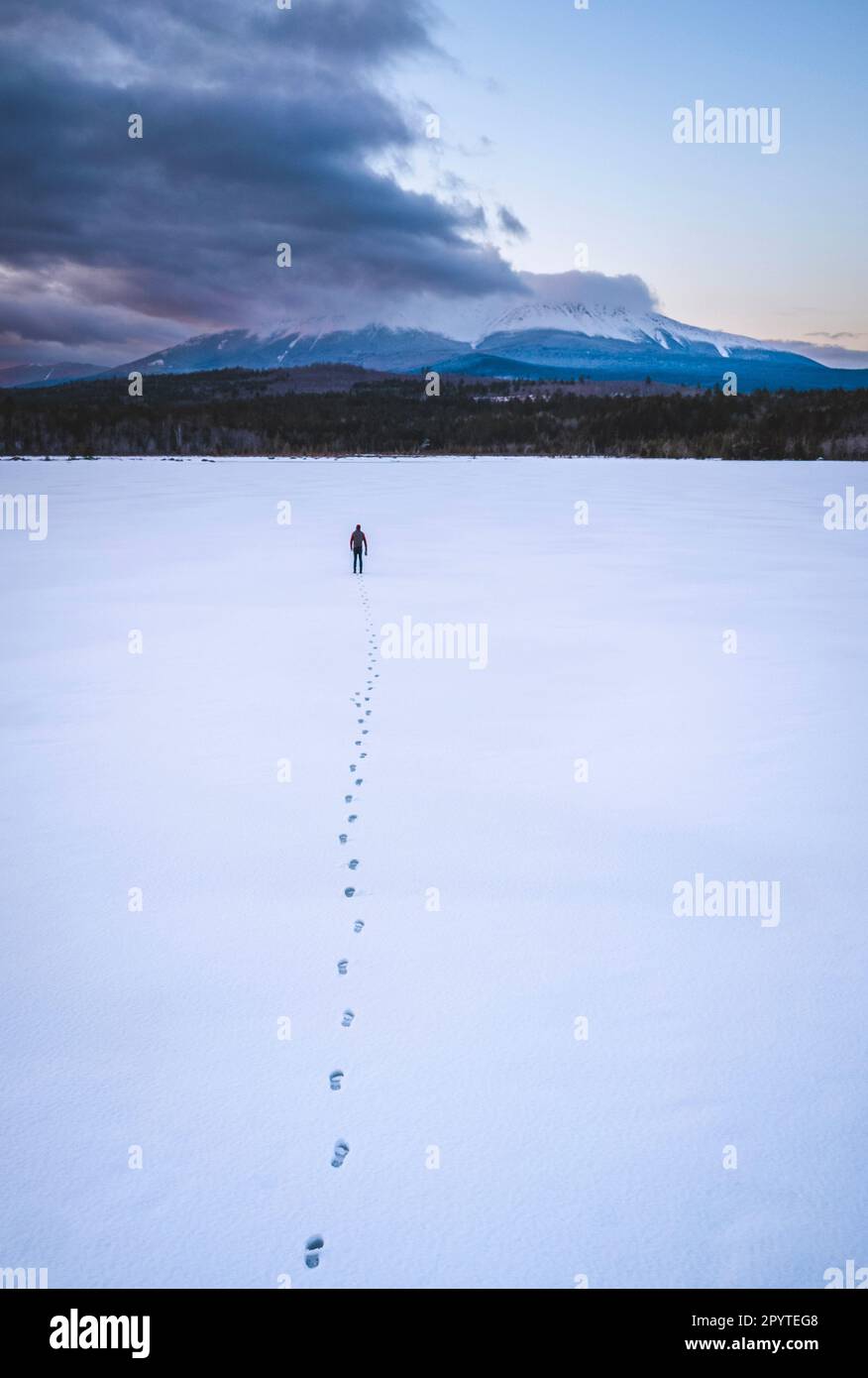 Lone man on lake ice with footsteps and mountain Stock Photo - Alamy