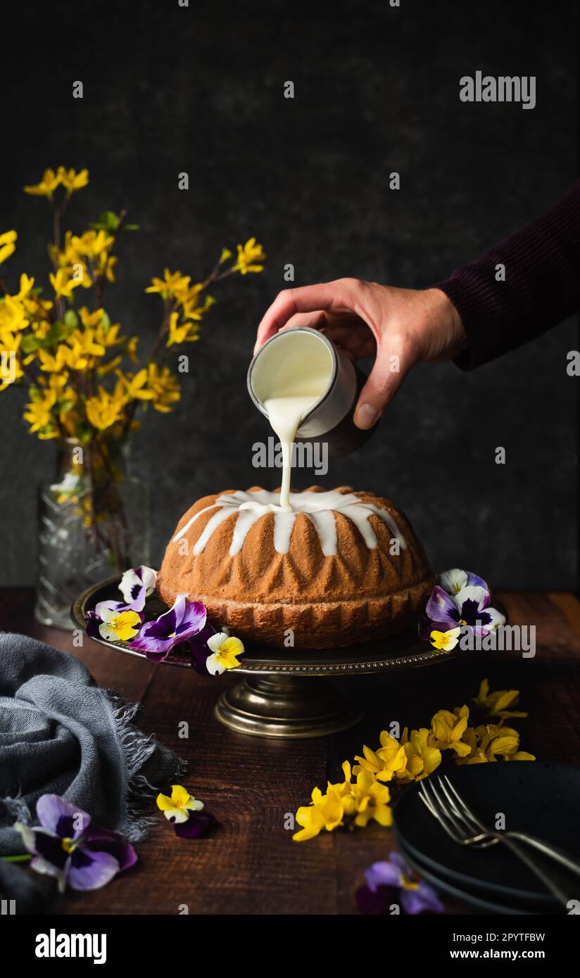 Hand pouring icing on bundt cake decorated with flowers Stock Photo - Alamy