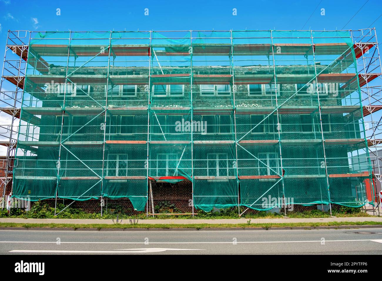 Scaffolding with green safety netting near a multi-story brick house ...